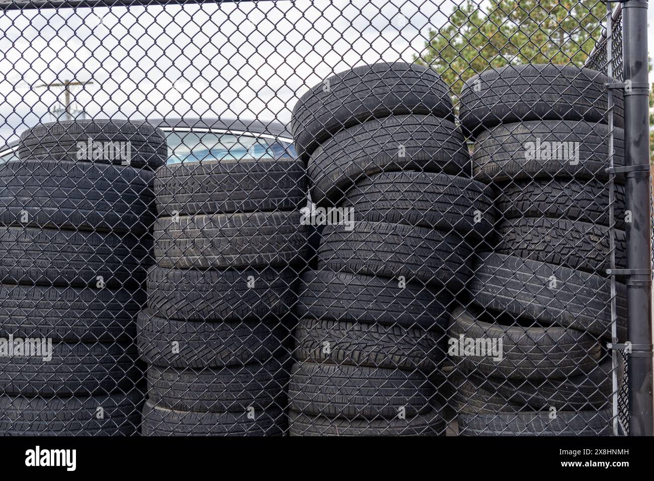 Used tires stacked high - visible through chain-link fence - under gray ...