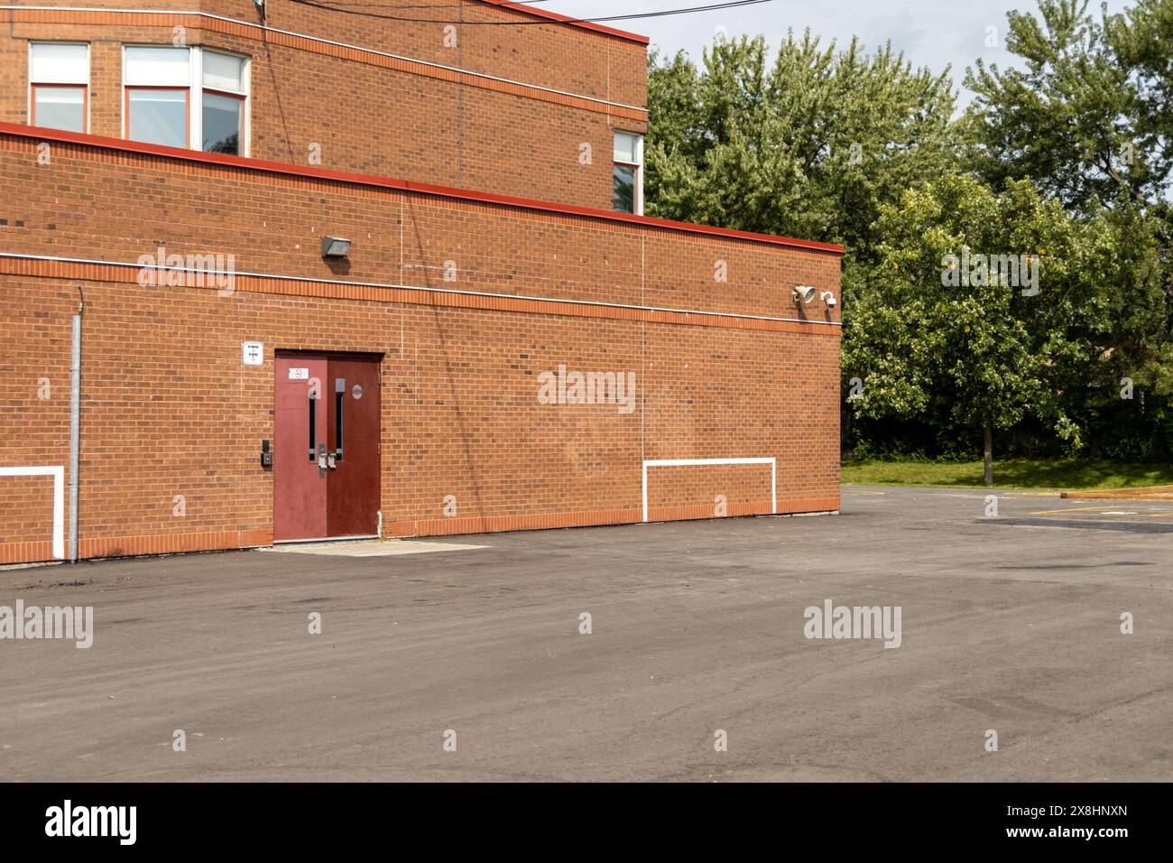 Brick building with red door - empty parking lot - green trees ...