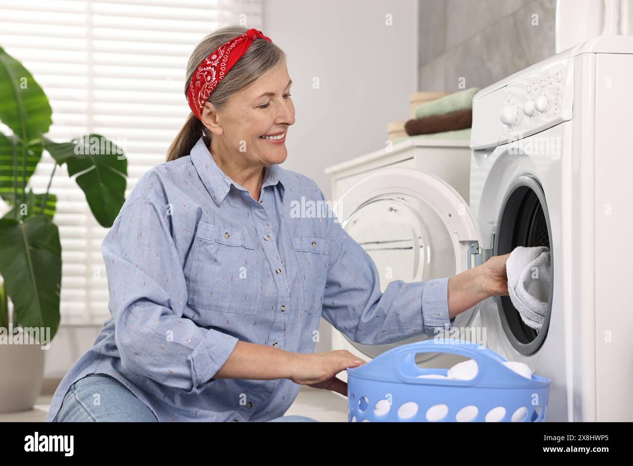 Happy housewife putting laundry into washing machine at home Stock ...