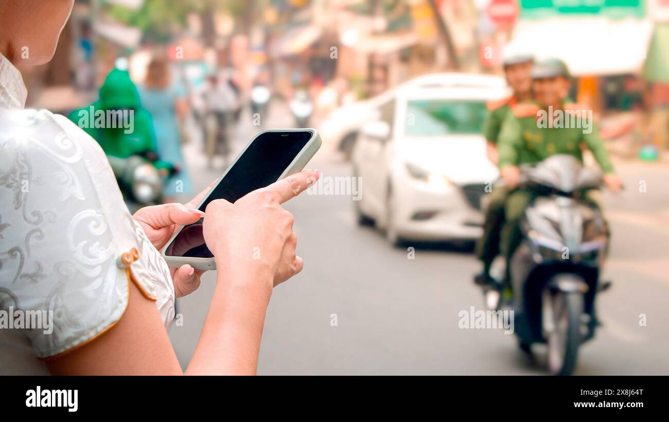 A woman is texting on her phone in a busy street with Vietnamese police ...