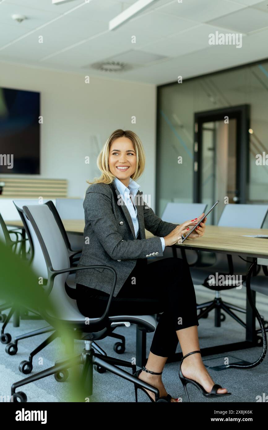 A focused woman in business attire efficiently works on a tablet in a ...