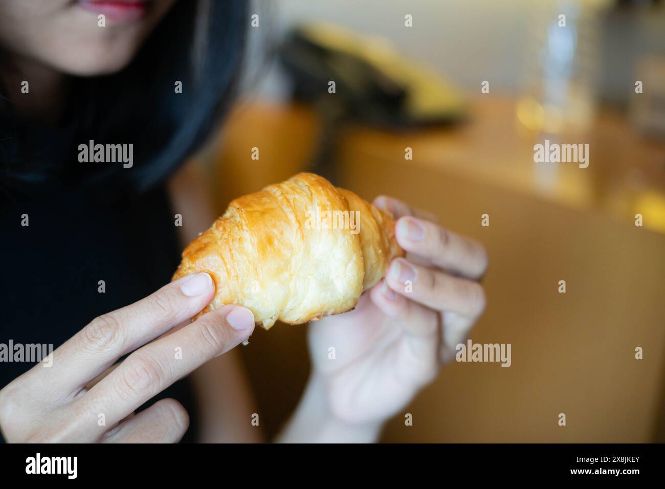 A person holding a croissant with both hands, partially visible face ...