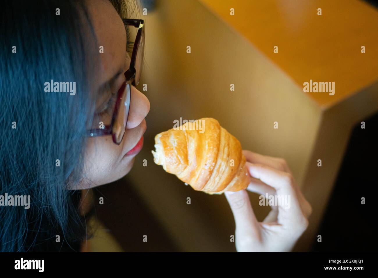A person with glasses holding and about to eat a croissant Stock Photo ...