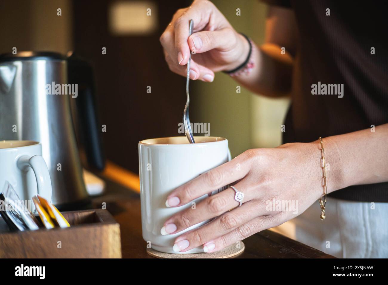 Close-up of a person stirring a drink in a white mug with a spoon. The ...