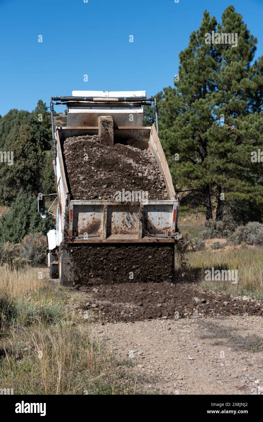 Old, white dump truck laying gravel on a road in a remote part of ...