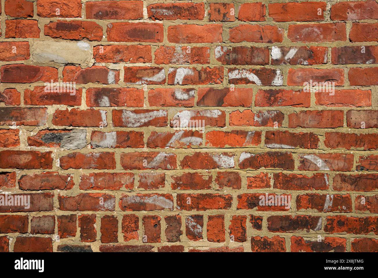 Horizontal and vertical red brick wall with faded graffiti on the ...