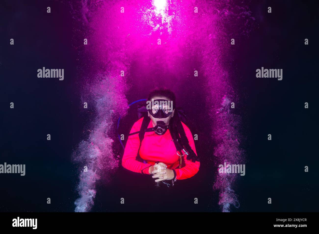 A female scuba diver relaxes into a night dive as explosions of pink ...