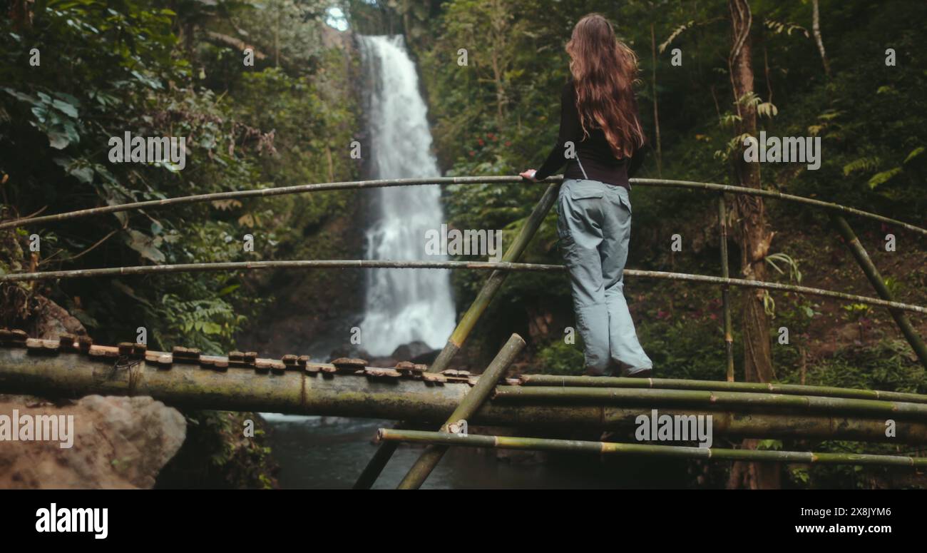 A woman stands confidently on a wooden bridge facing a majestic ...