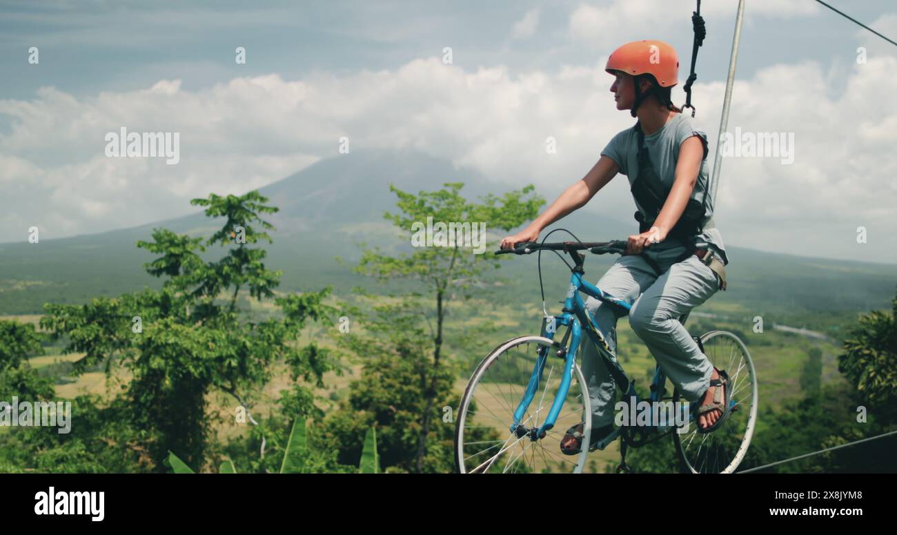 A womani riding a bike on top of a zip line over the beautiful volcanic ...