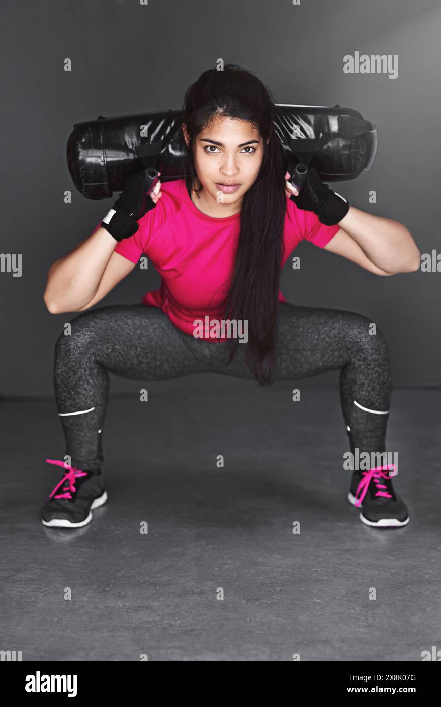 Woman, athlete and sandbag squat in studio or glutes muscle or exercise ...