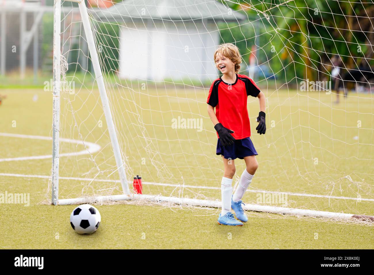 Kids play football on outdoor field. Little goalkeeper in goal ...
