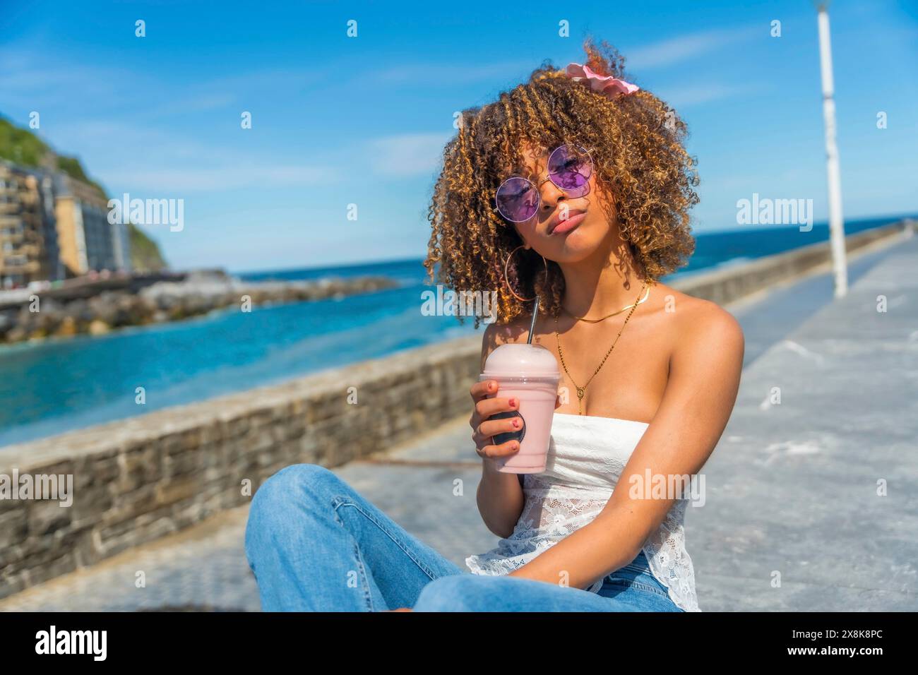 Cool latin young woman with curly hair in summer clothes drinking a ...