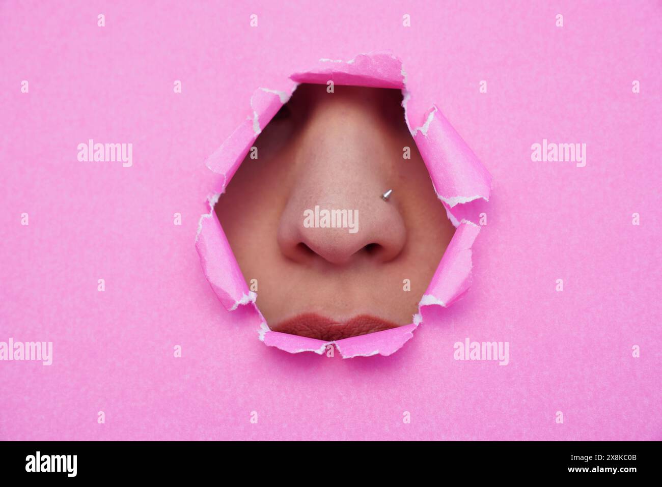 A woman's nose and mouth are visible through pink torn paper Stock ...