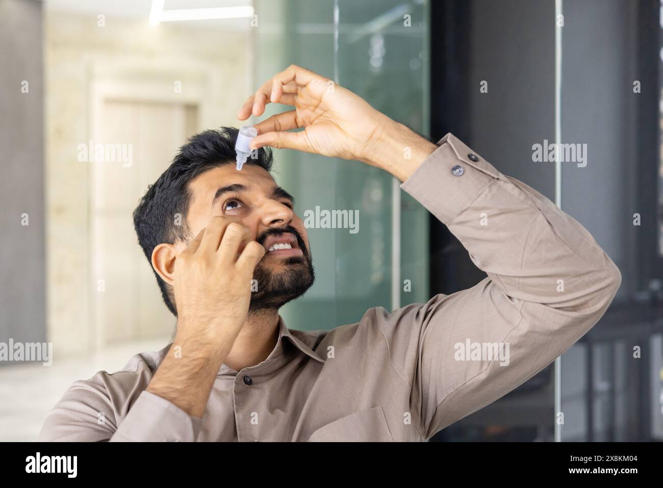 A man indoors carefully applying eye drops to maintain clear vision ...