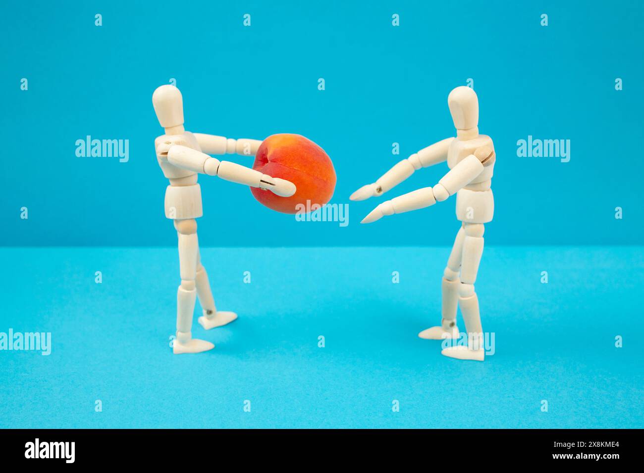 Two wooden mannequins, one holding a peach fruit, giving or donating ...