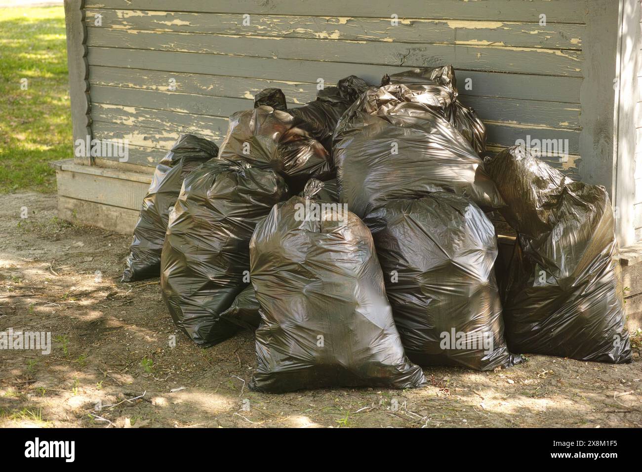 A pile of black plastic garbage bags full of trash standing near wooden ...