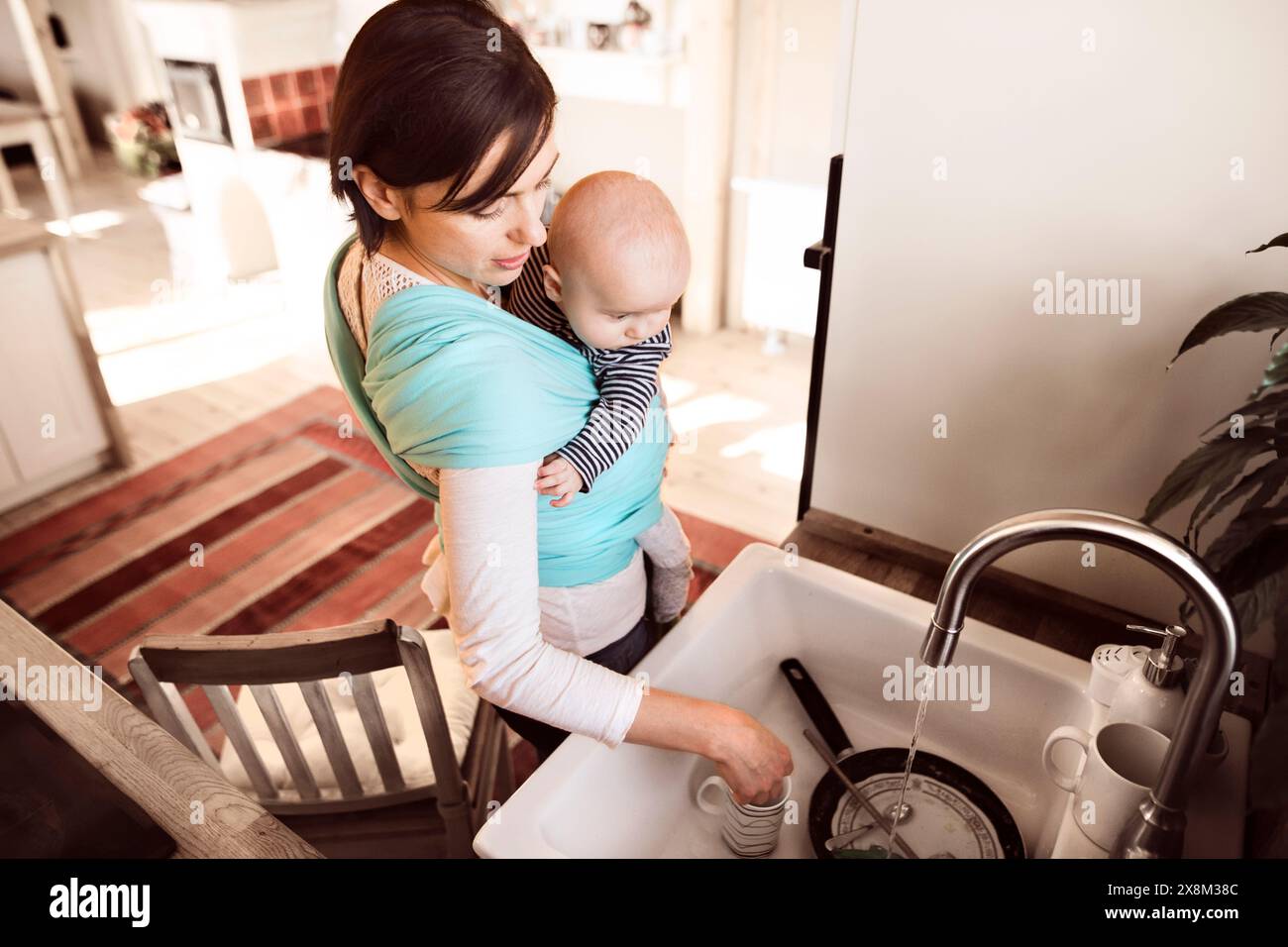 Mother holding small baby while cleaning dishes, carrying him around ...