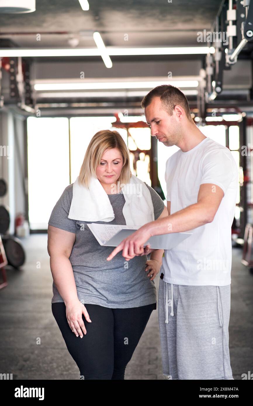 Overweight woman consulting with trainer, discussing daily workout plan ...