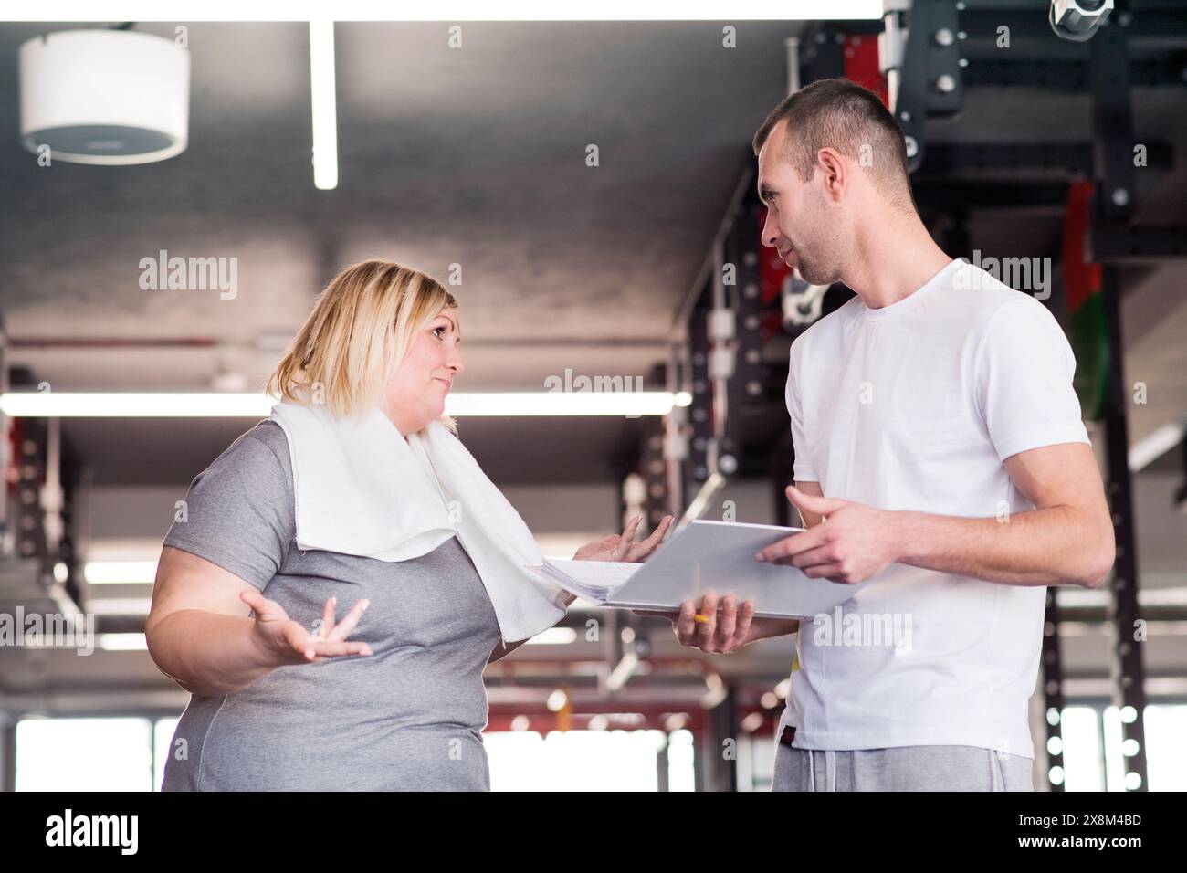 Overweight woman consulting with trainer, discussing daily workout plan ...