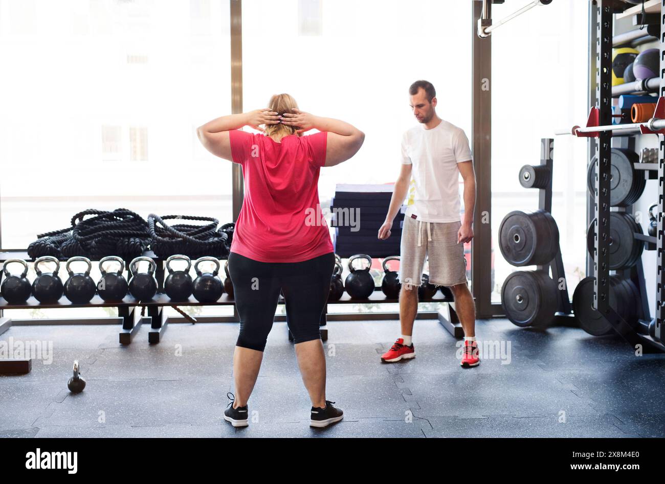 Overweight woman exercising in gym. Personal trainer couching her and ...