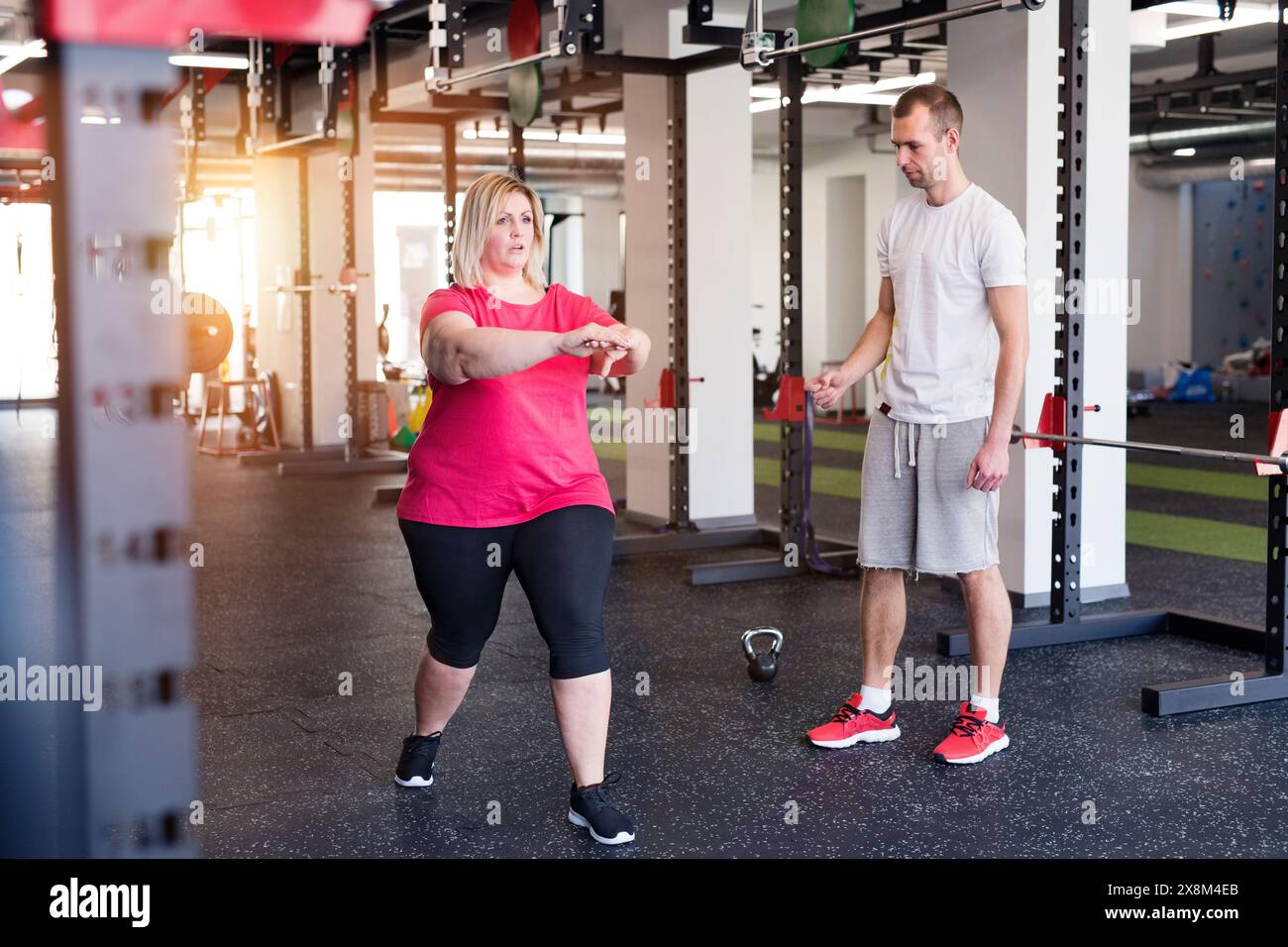 Overweight woman exercising in gym. Personal trainer couching her and ...