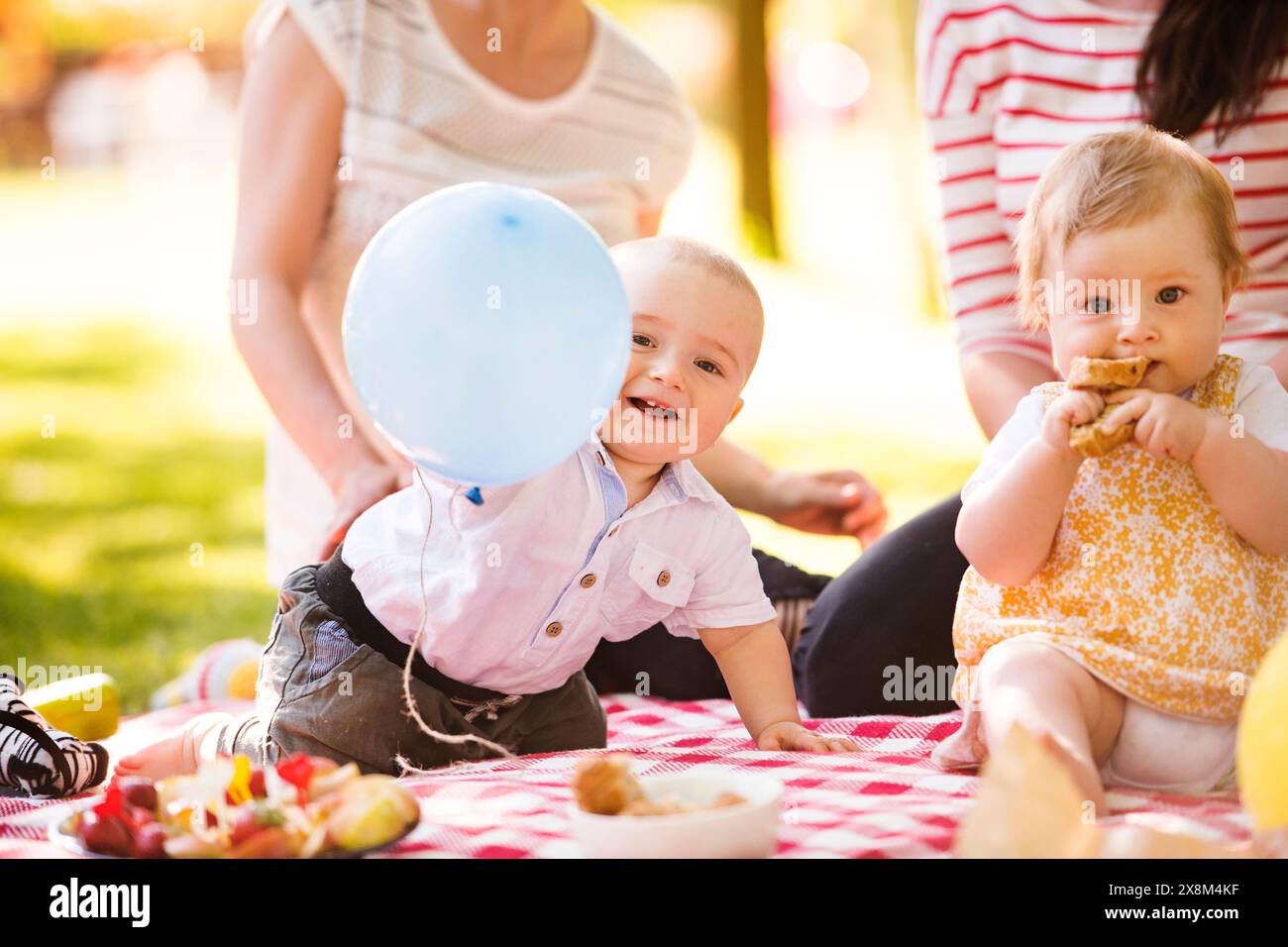 Mothers and babies enjoying group picnic outdoor in park, sitting on ...