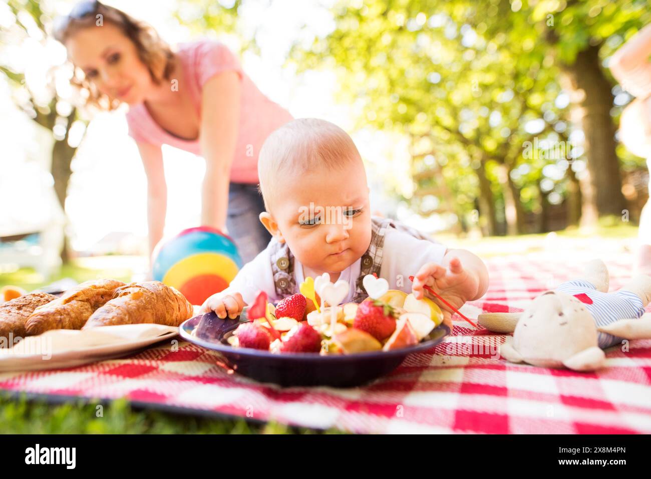 Mothers and babies enjoying group picnic outdoor in park, sitting on ...