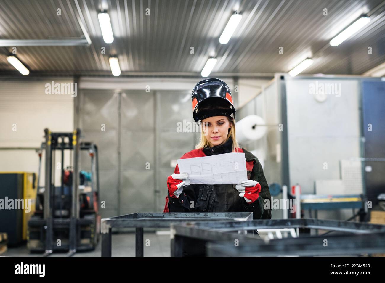 Beautiful blonde woman works as a welder in workshop, reading ...