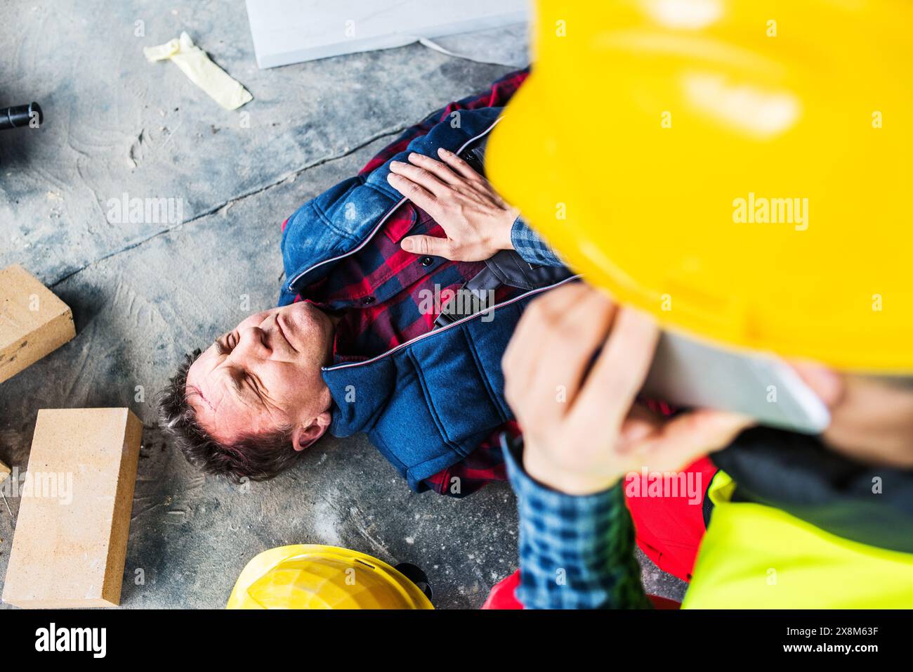 Colleague giving first aid to unconscious worker after accident ...