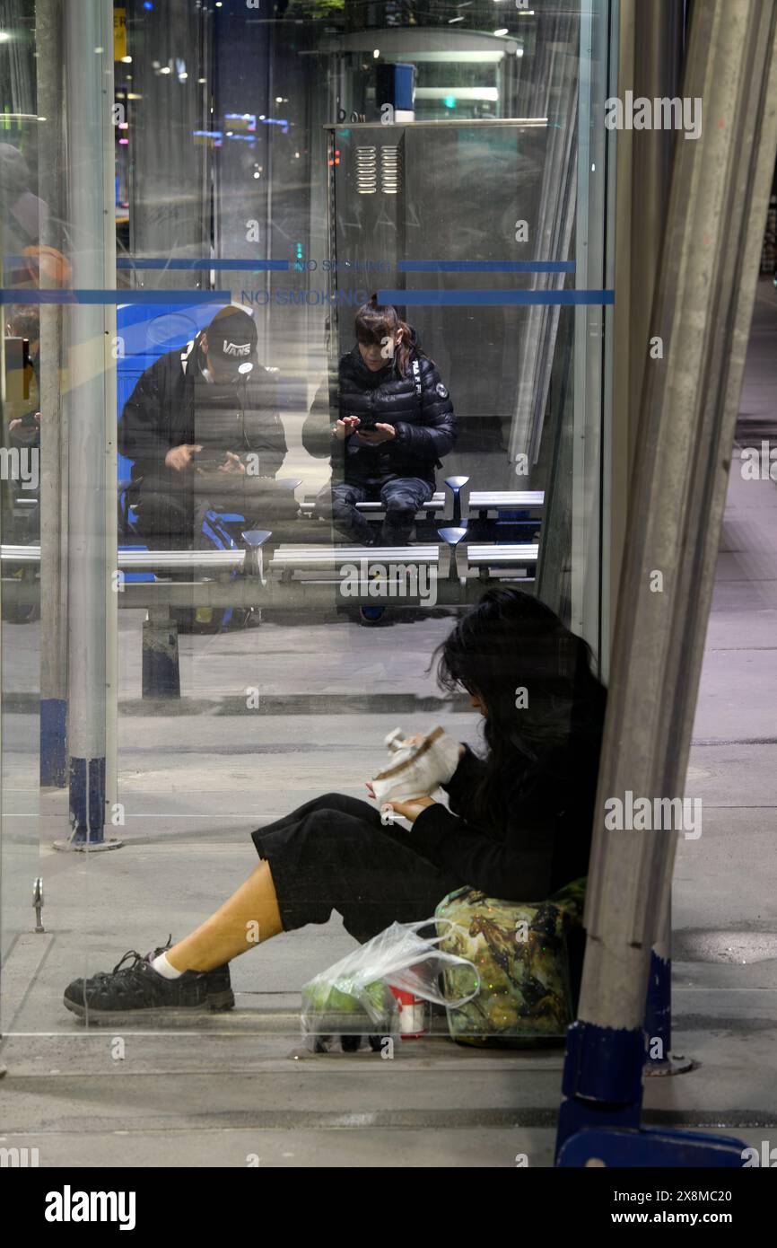 People waiting at a light rail transit station in nighttime downtown ...