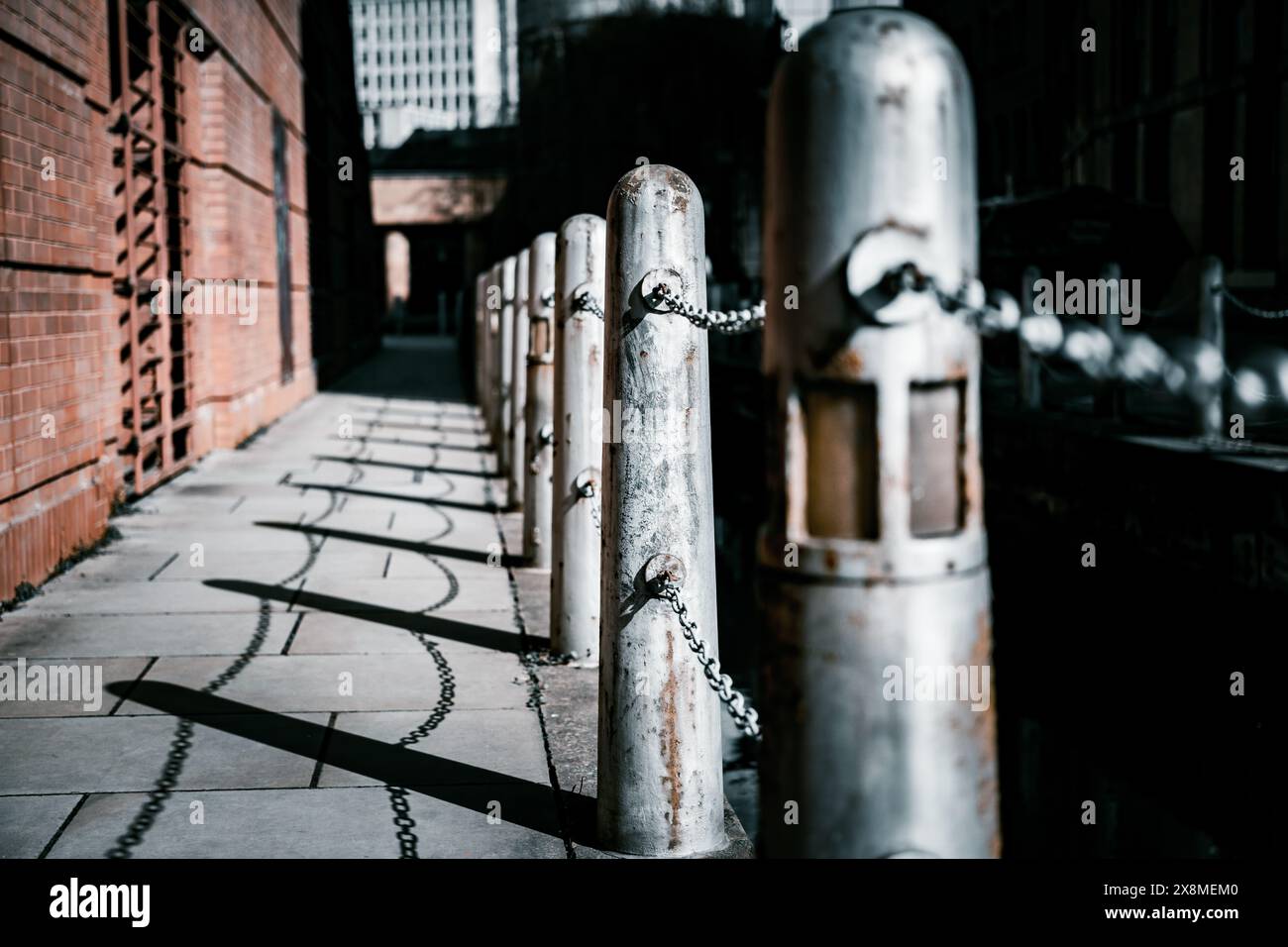 An Urban pathway with metal posts and chains, long shadows. Brick ...