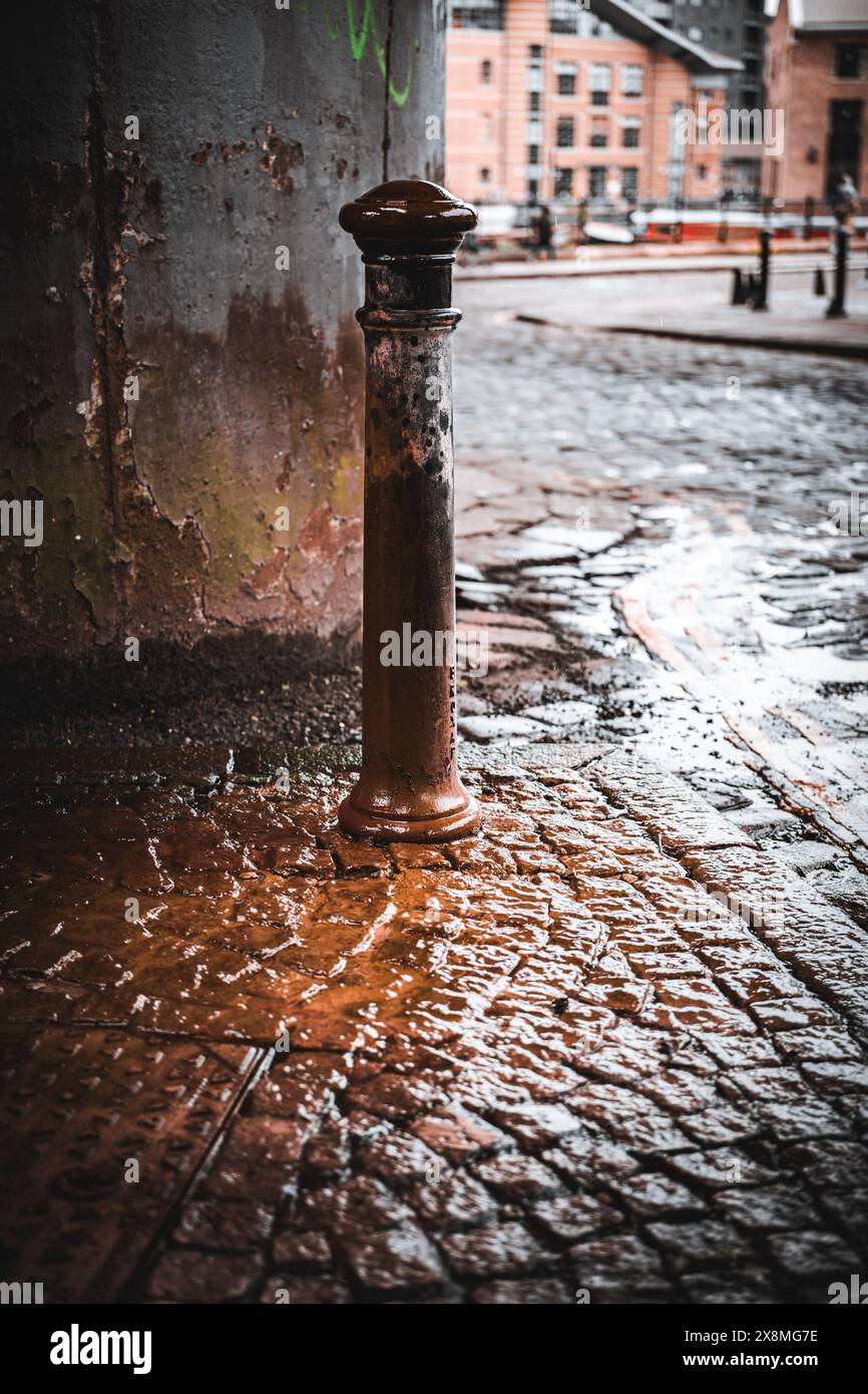Rustic, rain-soaked cobblestone street with an old rusty metal bollard ...