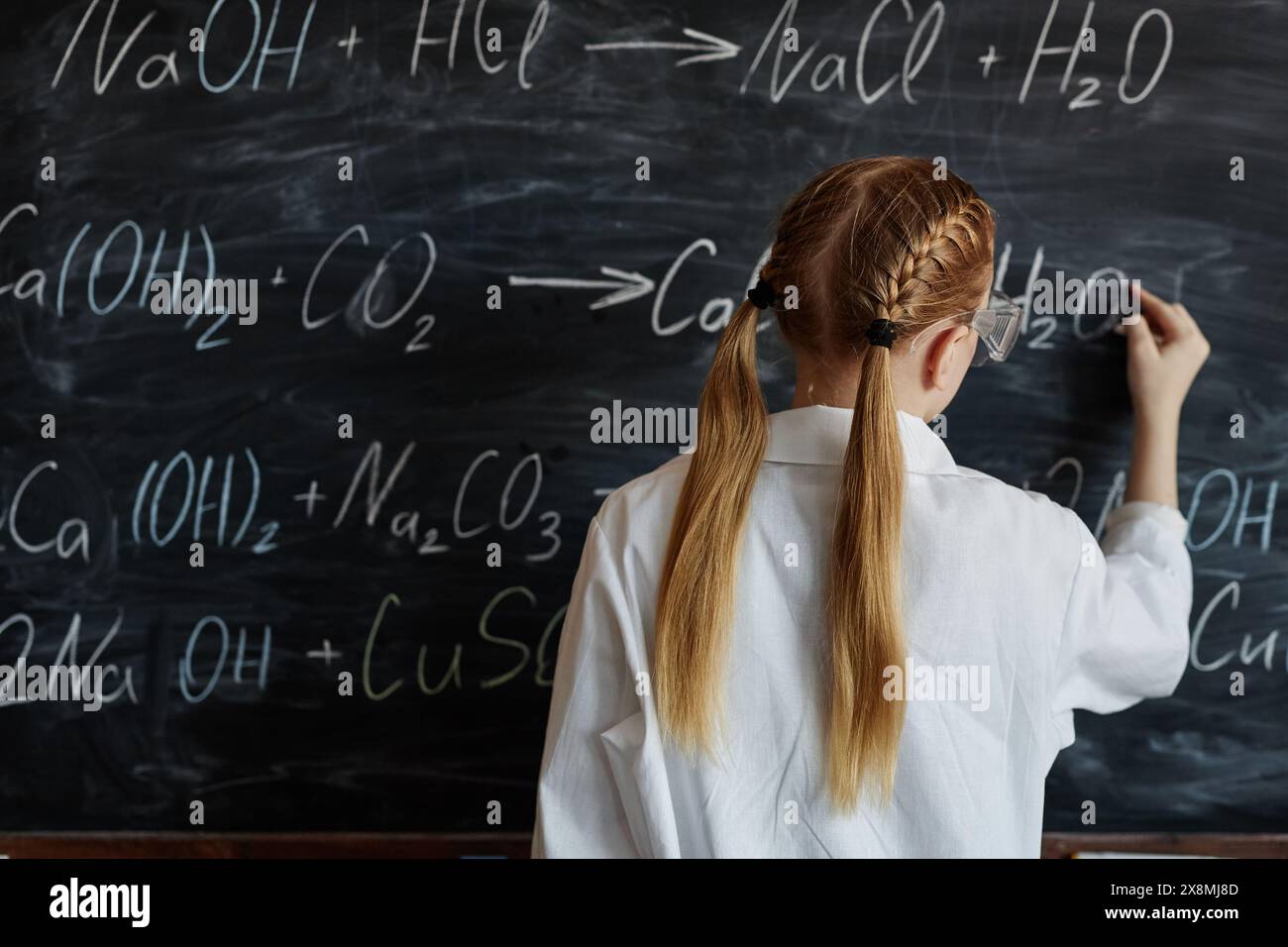 Rear view of unrecognizable schoolgirl wearing white lab coat writing ...