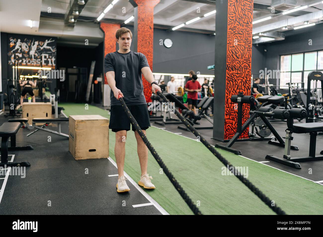 Portrait of beginner sportsman doing battle ropes functional training ...