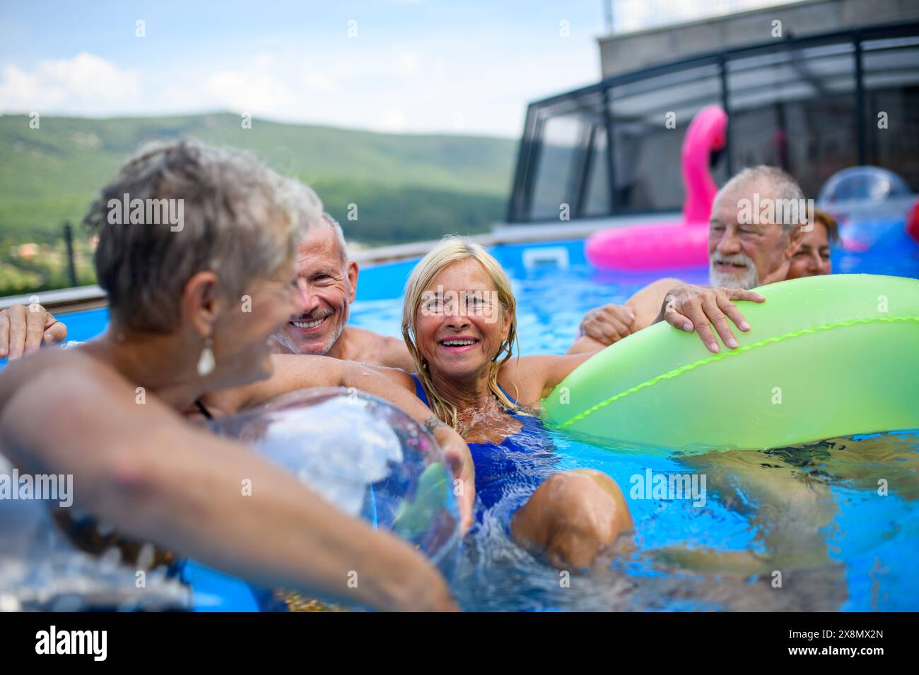 Group of cheerful seniors shaving fun in pool jumping, swiming and ...