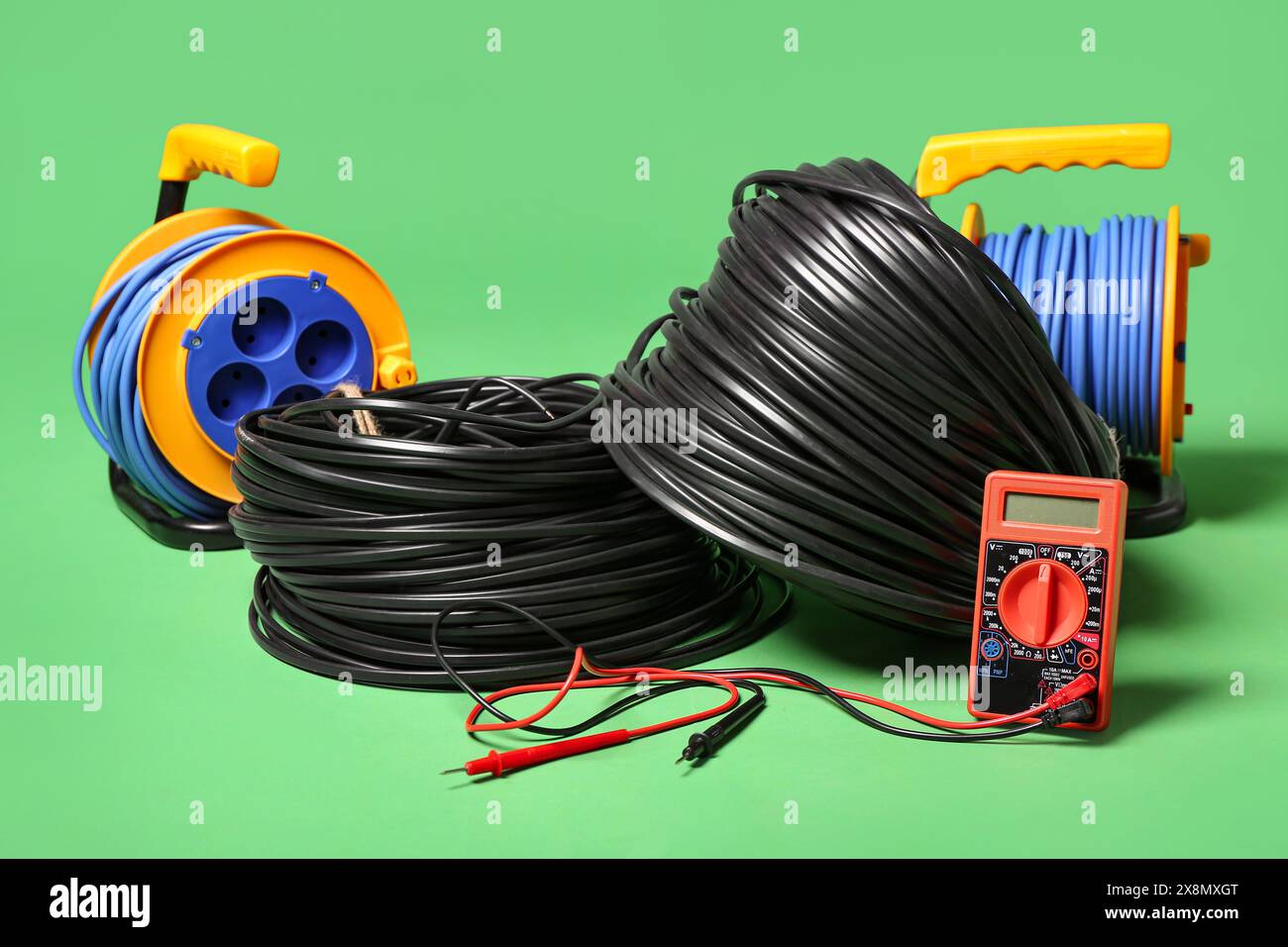 Rolled cables, multimeter and extension cable reels on green background ...