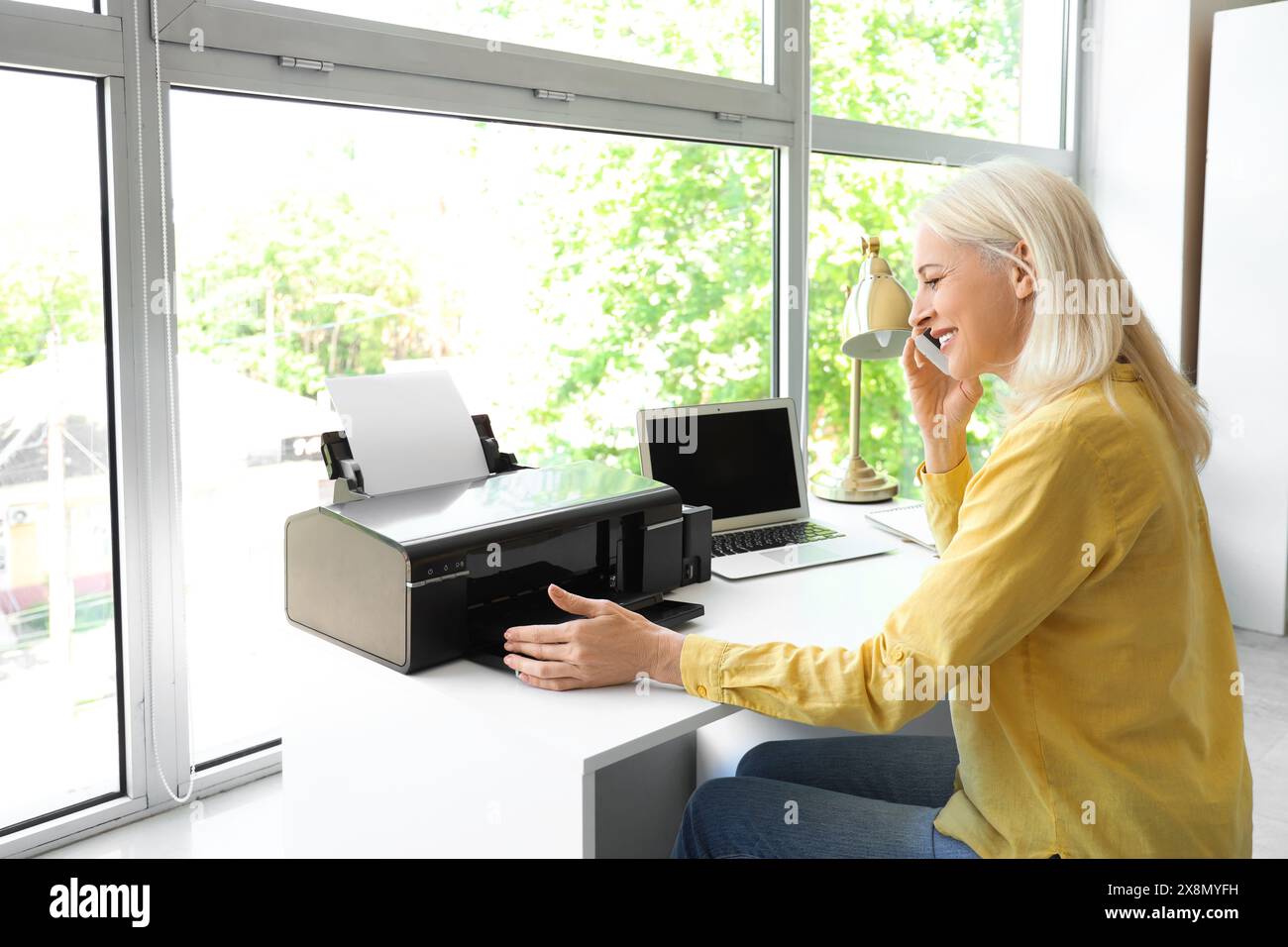 Mature woman with printer talking by mobile phone at home Stock Photo ...