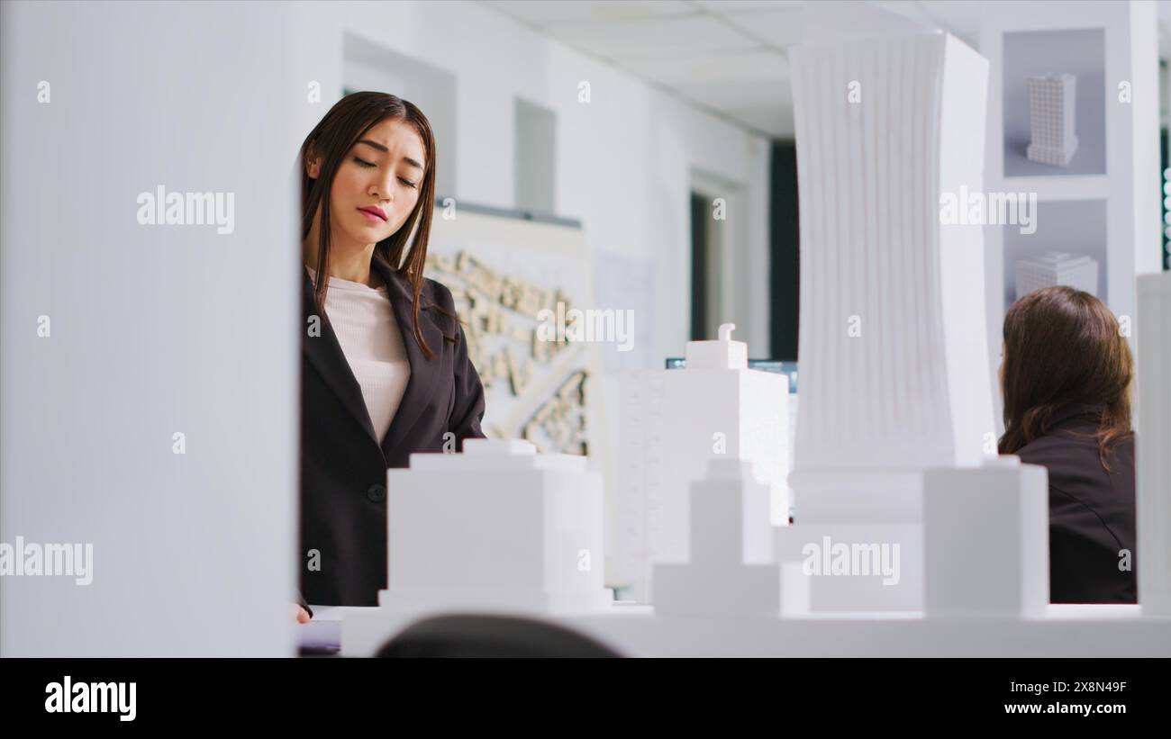 At design table, engineer reviews schematics and 3D construction plans ...