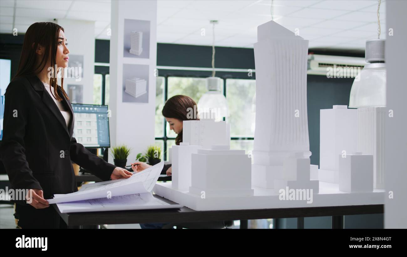 Architecture office employee looking at building model, working with ...