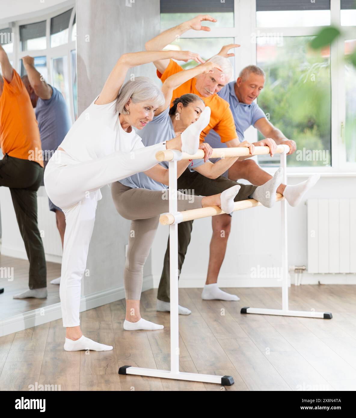 Active mature woman practicing leg stretching holding by ballet barre ...