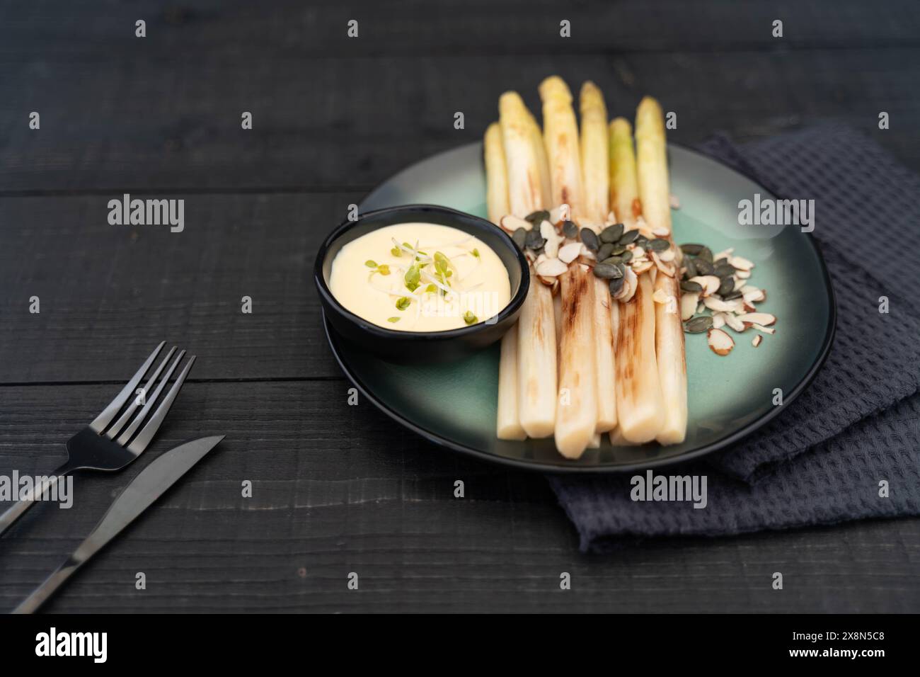 Green asparagus served on dark plate alongside sauce hollandaise ...