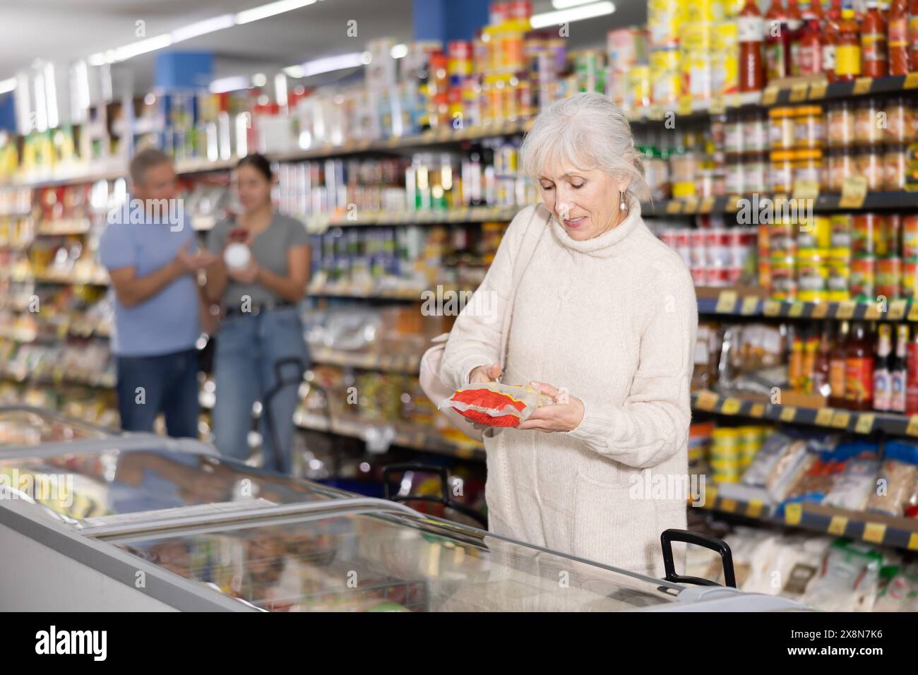 Mature woman choosing frozen food in supermarket. Young woman ...