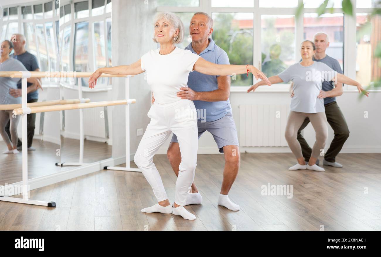 Mature woman practicing plie position in pair with man in dance studio ...