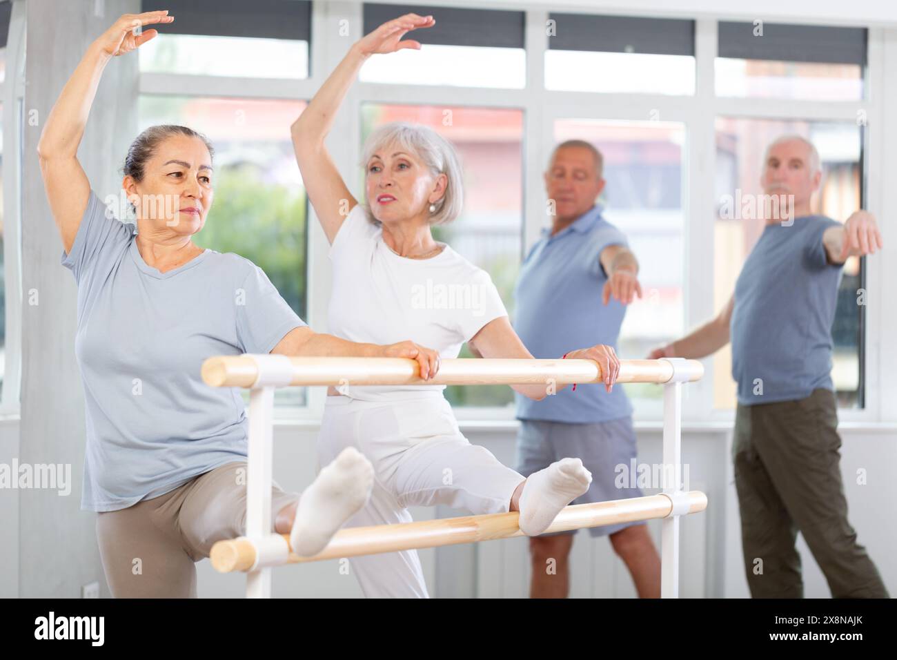 Elderly women with group of dancers practicing ballet pose grand batman ...