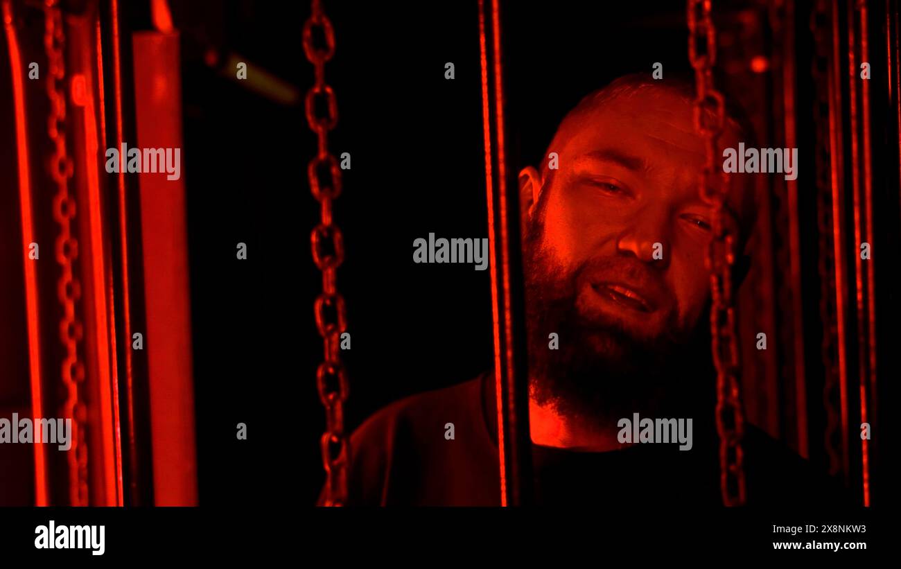 Stylish bearded man dancing by hanging chains in colorful neon light in night club. Media ...