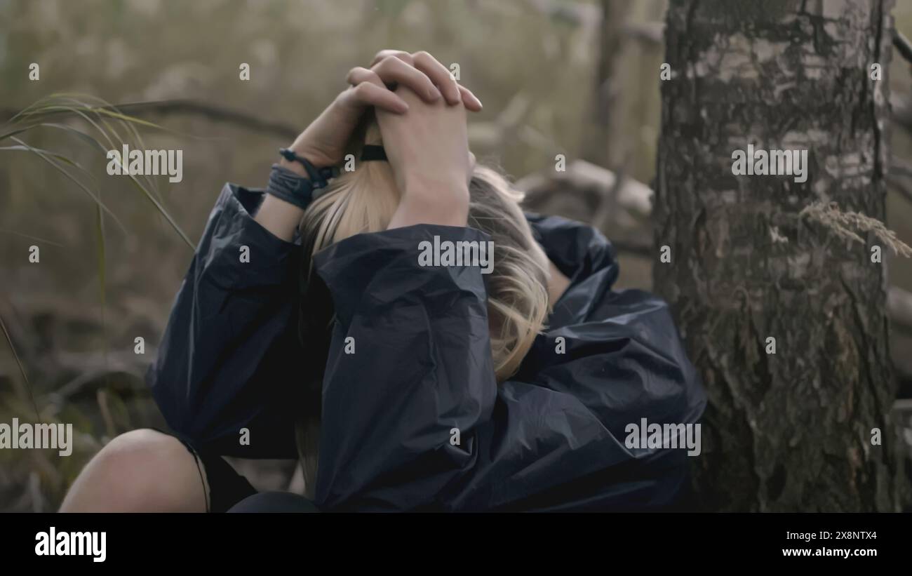 Young man sits tired by tree in forest. Stock. Young man is lost in ...