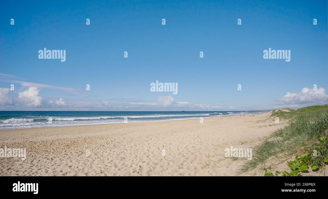 A sunny day at the beach with sandy foreshore, crashing surf waves and ...