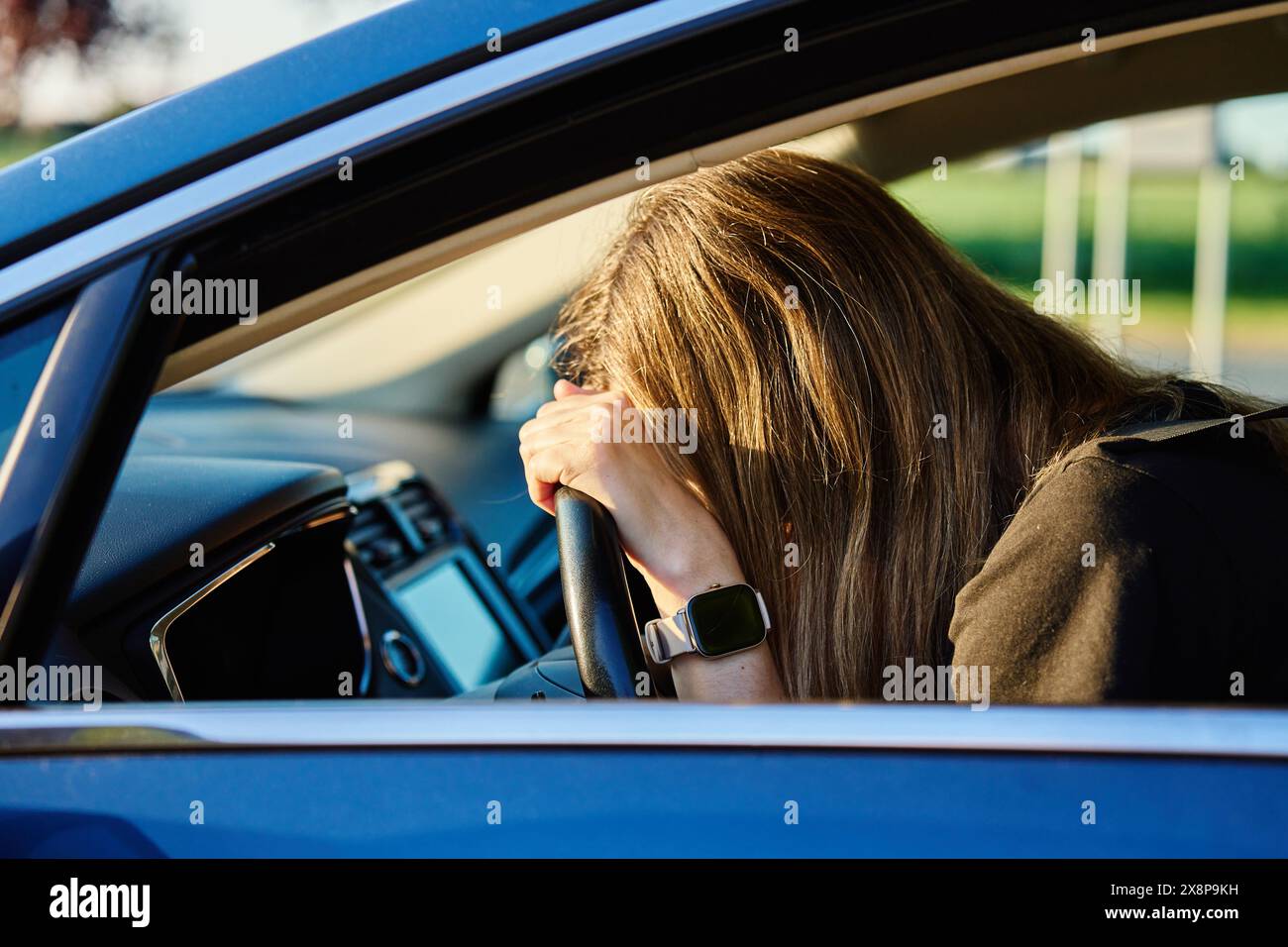 Woman is seated inside car with her head resting on steering wheel ...