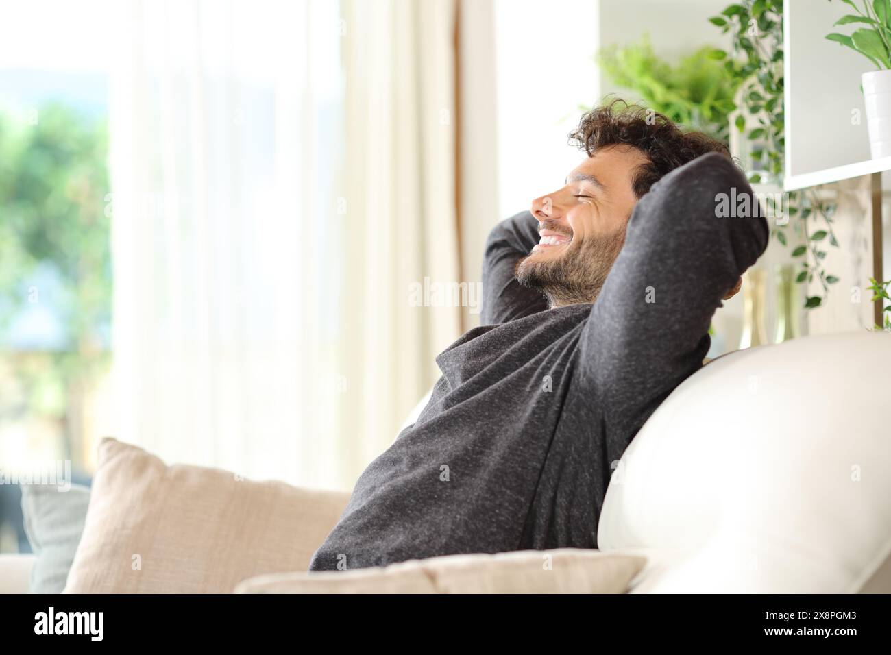Side view portrait of a happy man sitting on a couch relaxing at home ...