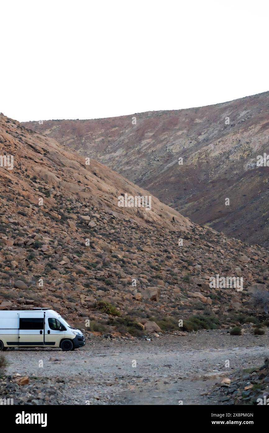 A lone camper van rests at the base of rocky, barren mountains ...